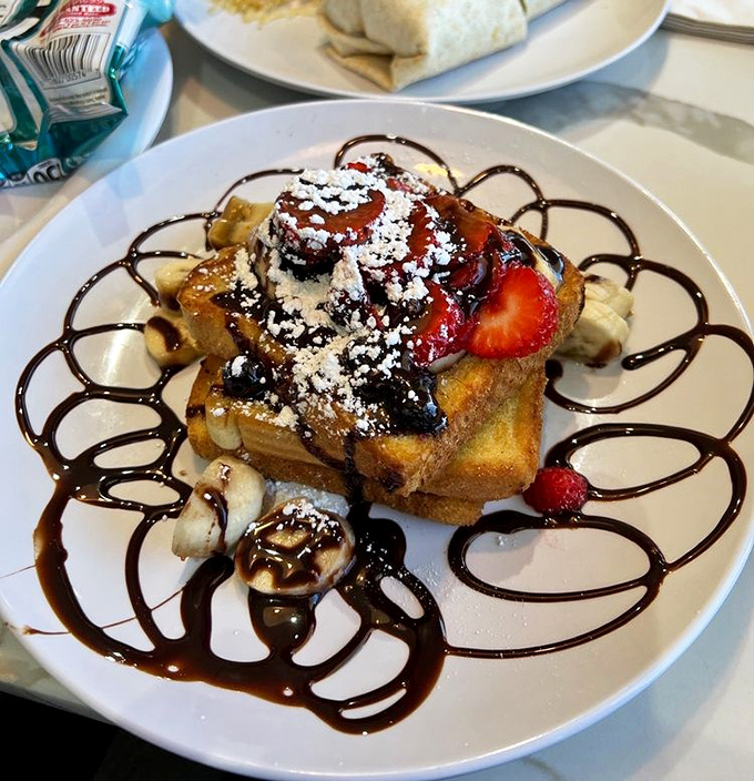 French toast elevated to art form&mdash;bananas, strawberries, chocolate drizzle, and powdered sugar create a breakfast that's basically dessert with permission.