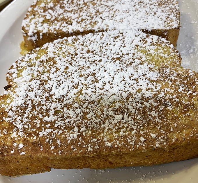 French toast dusted with powdered sugar sits like a golden island on the plate &ndash; simple perfection that needs no passport to transport you to breakfast bliss.