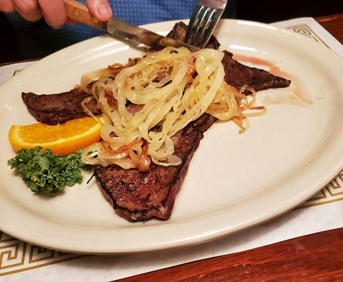 This steak arrives with a mountain of perfectly grilled onions, a citrus garnish, and the promise of a nap afterward.