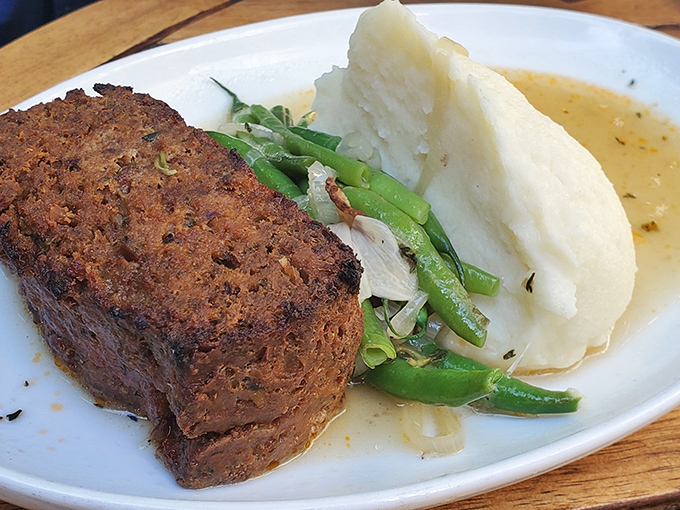 Meatloaf reimagined: a hearty slice of nostalgia served with creamy mashed potatoes and vibrant green beans in a pool of savory gravy.