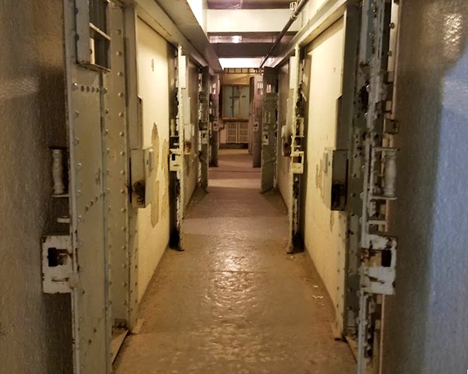 Imagine the echoing footsteps of guards patrolling this narrow corridor, checking cells where inmates marked time in cramped quarters behind heavy doors.