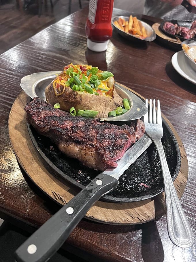 A perfectly seared steak resting on its sizzling throne, accompanied by a loaded baked potato that's dressed better than most people at the mall.