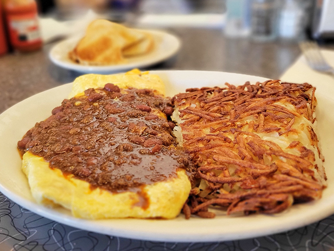 Breakfast perfection doesn't need to be complicated—just eggs smothered in chili alongside hash browns that could make a potato proud.