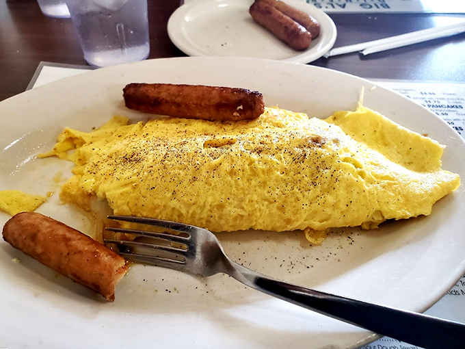 An omelet so perfectly executed it deserves its own gold medal. Those sausages standing guard? They're not just sides—they're breakfast bodyguards.