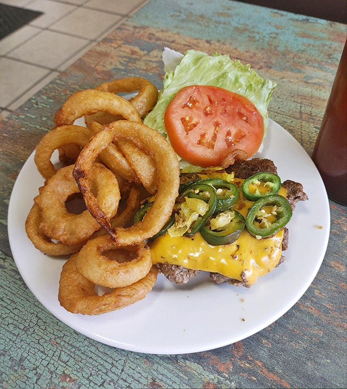 Golden onion rings frame a burger topped with melty cheese and jalape&ntilde;os. A symphony of crunch, spice, and satisfaction on a classic white plate.