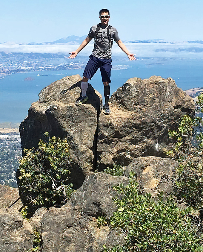 A hiker celebrates reaching a viewpoint that makes apartment security deposits seem reasonable again&mdash;fog-shrouded Bay Area splendor worth every step.