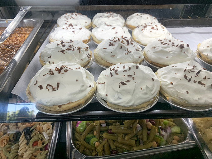 Dessert pies lined up like beauty pageant contestants, each crowned with a swirl of frosting and chocolate shavings, waiting for their moment in the spotlight.