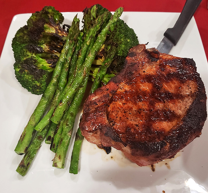 A pork chop that's seen the right side of fire, nestled alongside asparagus that somehow steals a bit of the spotlight.