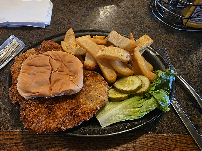 The legendary pork tenderloin sandwich in its natural habitat—crispy edges extending beyond the bun like a solar eclipse of deliciousness.