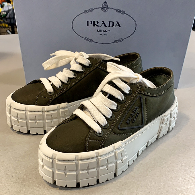 Prada sneakers with their distinctive chunky soles sit patiently in their box, whispering, "You know you've always wanted us, and now you can afford us."