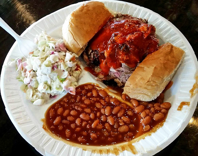 A pulled pork sandwich so generous it needs structural engineering, with coleslaw and beans playing worthy supporting roles.
