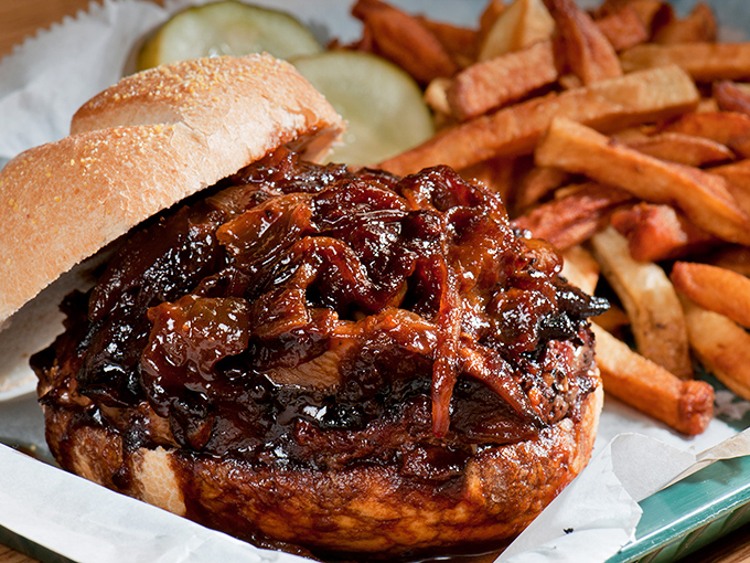 This isn't just a sandwich; it's an architectural marvel of pulled pork, sauce, and bun – with sweet potato fries standing guard.