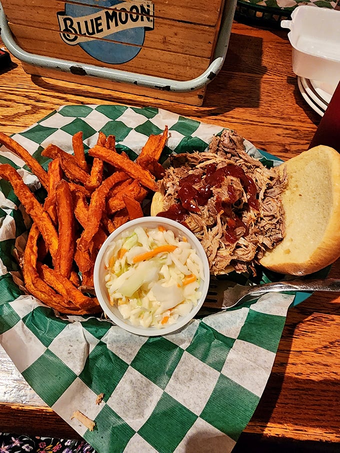 Sweet potato fries, tangy slaw, and pulled pork on a checkered paper &ndash; the holy trinity of BBQ satisfaction. Blue Moon in the background suggests divine pairing.
