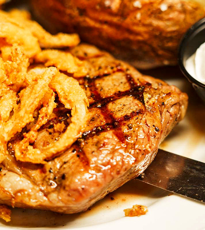 This ribeye doesn't just sit on the plate&mdash;it commands attention with perfect grill marks and a crown of crispy onions.