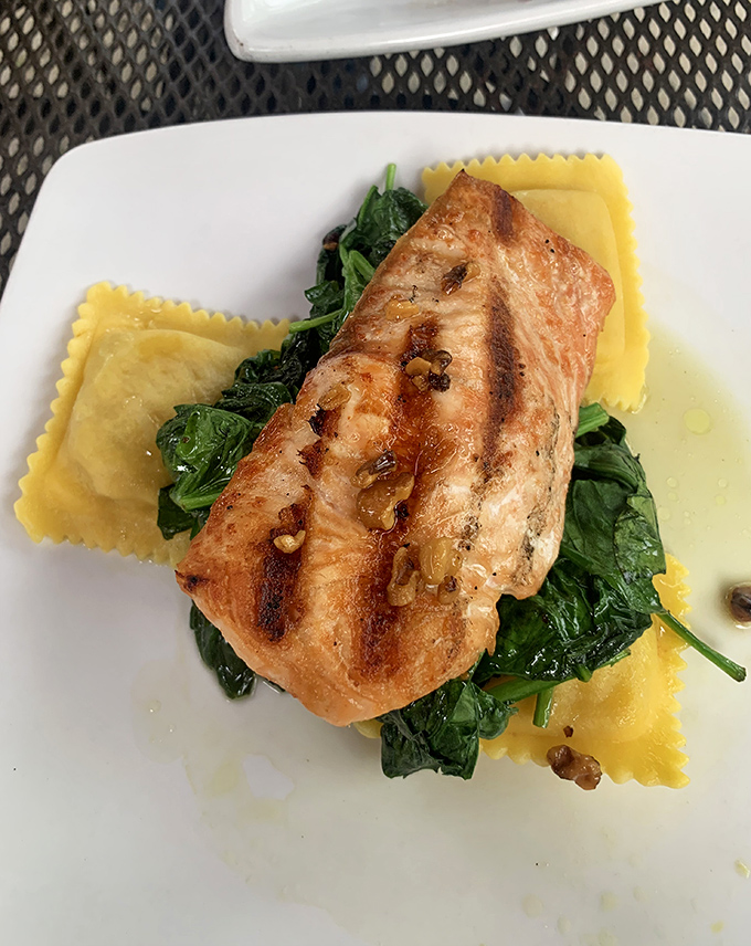 Perfectly seared salmon resting on a bed of spinach and ravioli &ndash; proof that tavern food can dance gracefully between rustic and refined.