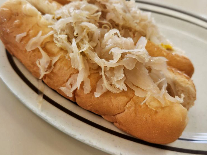 The sauerkraut dog rests on its simple white plate like royalty—tangy, savory proof that sometimes the classics need no improvement.