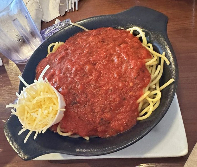 Spaghetti served on a sizzling skillet with marinara generous enough to make an Italian grandmother nod in approval. Cheese on standby, ready for its supporting role.