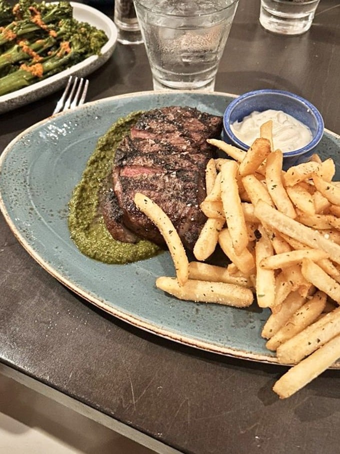 Steak Frites done right is culinary poetry—this perfectly seared cut resting on herb-infused sauce with golden fries standing at attention nearby.