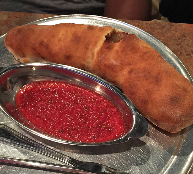 The golden-brown calzone, accompanied by vibrant marinara, is the pizza's sophisticated cousin—all the flavors tucked into one portable package.