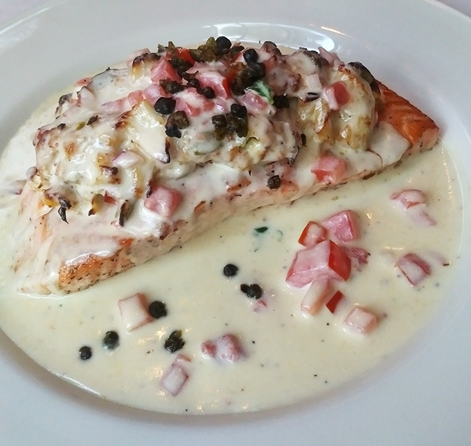 This salmon isn't just topped with sauce—it's wearing a tuxedo of creamy goodness studded with capers and diced ham. Ocean meets artistry.