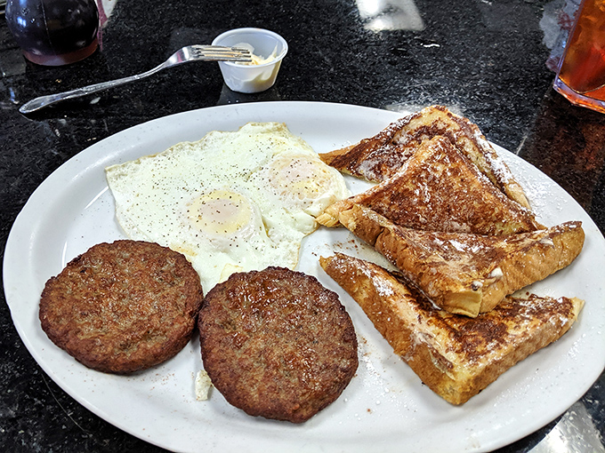 The breakfast trinity: golden-brown sausage patties, eggs with just-right yolks, and French toast that puts ordinary bread to shame.