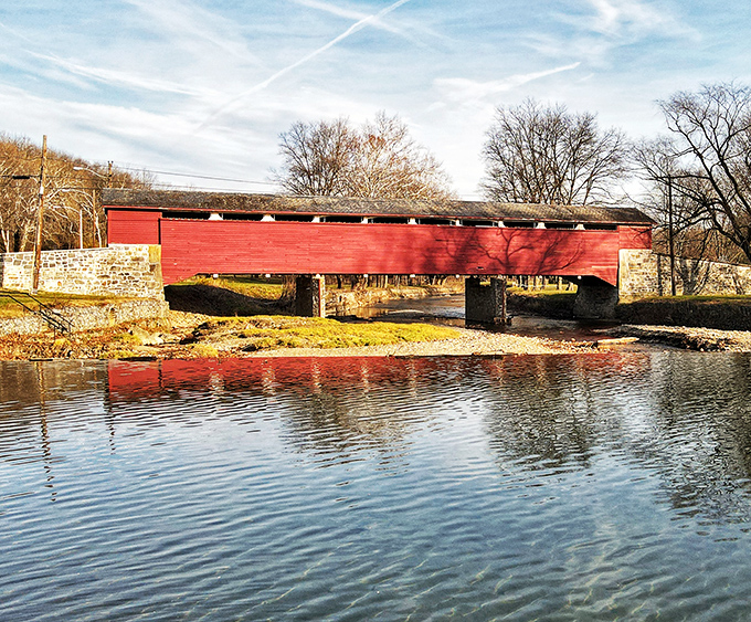 The bridge's reflection creates a perfect symmetry in Jordan Creek's waters, doubling the visual impact of this crimson landmark against the autumn landscape.