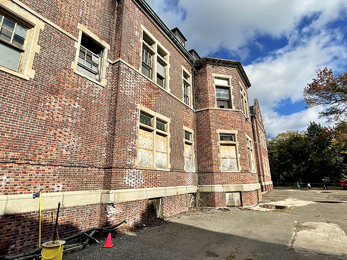 The weathered brick exterior, with its boarded windows and crumbling concrete, offers a textbook example of early 20th-century institutional architecture.