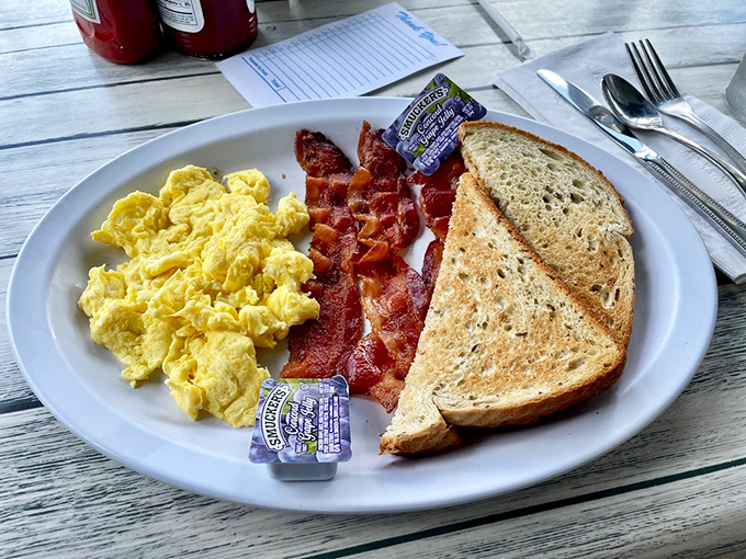 The breakfast trinity: fluffy scrambled eggs, perfectly crisped bacon, and toast that somehow makes you nostalgic for mornings at grandma's.
