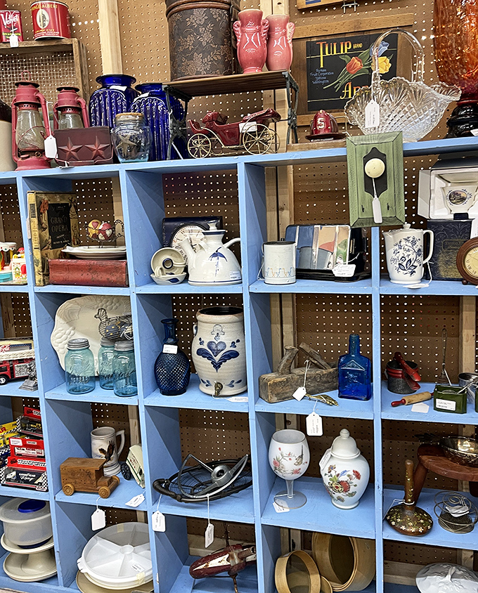 Blue cubby shelves showcase a perfectly curated chaos of vintage kitchenware, where your grandmother's favorite pitcher might be hiding in plain sight.
