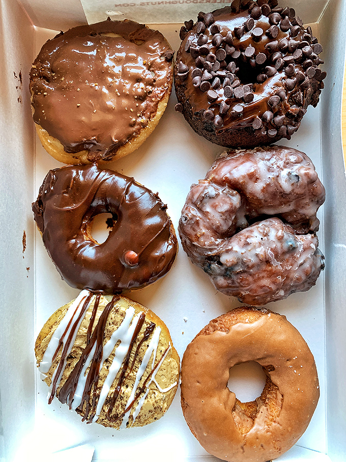 The donut box opens like a treasure chest of possibilities. Six different paths to happiness, each one more tempting than the last.