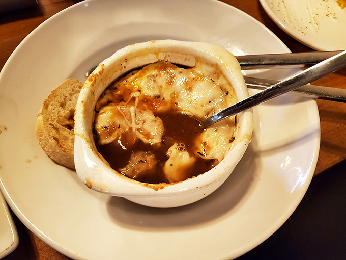 French onion soup that doesn't mess around—a rich broth with tender chunks of beef hiding beneath that glorious blanket of melted cheese. Spoon-licking inevitable.