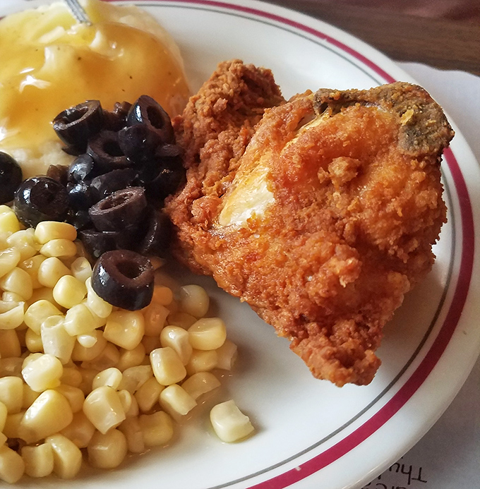 Golden-fried chicken that crackles when your fork touches it, sitting alongside corn and olives like they're all old friends at a delicious reunion.