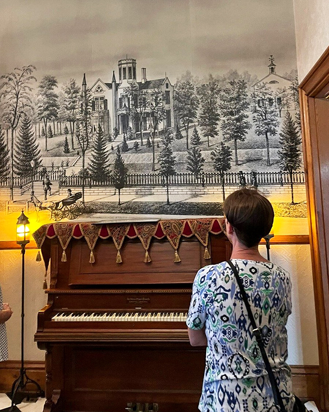 Music and history harmonize beautifully as a visitor admires the antique piano beneath a historical illustration. Some notes never go out of style.