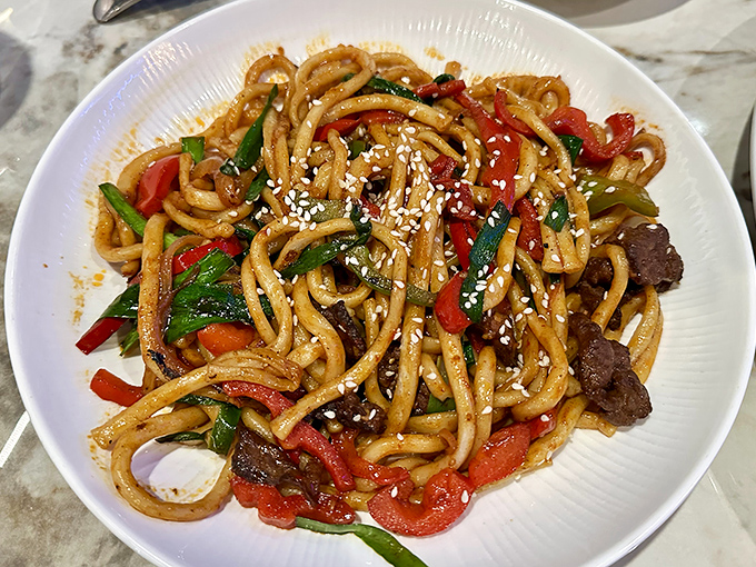 Hand-pulled noodles tossed with vegetables and meat create a colorful tangle that's part comfort food, part culinary artwork on a pristine white plate.