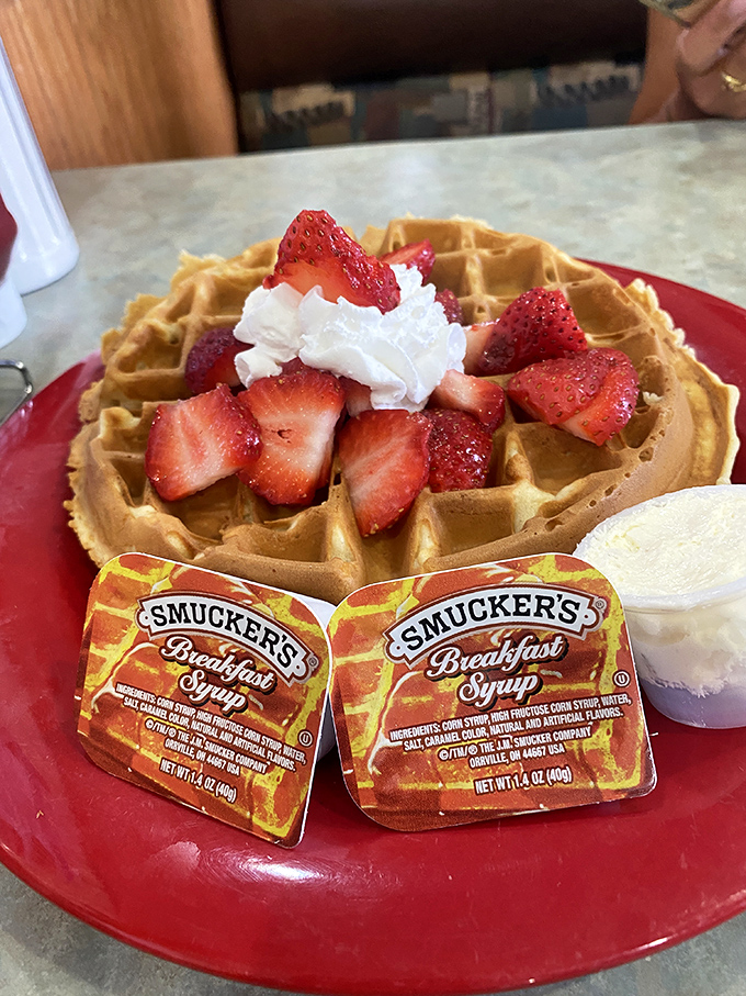 A waffle that's living its best life, adorned with fresh strawberries and whipped cream like it's dressed for the prom.