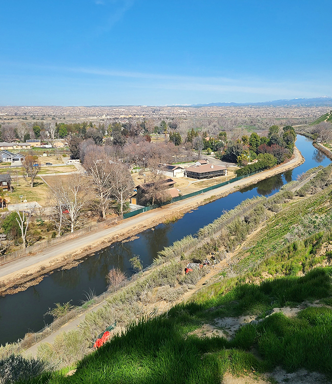 A peaceful canal winds through Bakersfield, with green hillsides, neighborhood homes, and wide-open views that stretch beautifully beneath California’s bright blue sky.