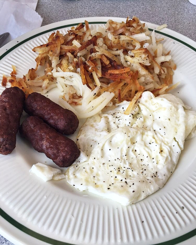The holy trinity of breakfast: perfectly crisped hash browns, sausage links with that satisfying snap, and eggs with yolks ready to create their own sauce.