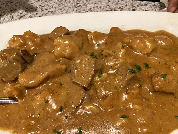 The beef goulash arrives like a savory lullaby – tender meat in rich paprika gravy that whispers, "Nap time approaches, but finish me first."