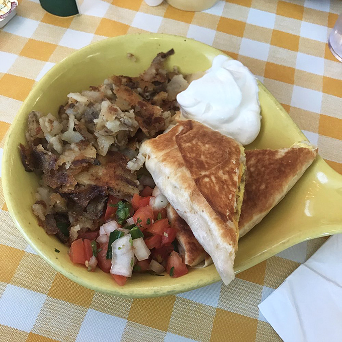 A hearty breakfast served on a sunny yellow plate &ndash; home fries, fresh pico, and a quesadilla that means business.