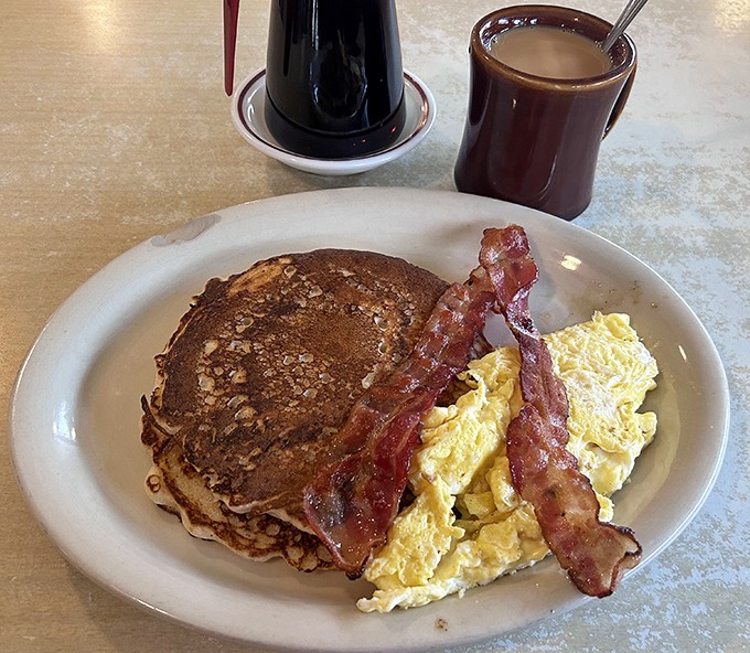 The holy trinity of breakfast: golden-brown pancake, scrambled eggs, and bacon so perfectly crisp it should win awards. Add coffee and you've found nirvana.