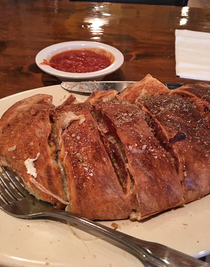 The calzone arrives like an edible treasure chest, its golden-brown exterior hiding a molten interior of cheese and fillings that's worth the inevitable chin dribble.