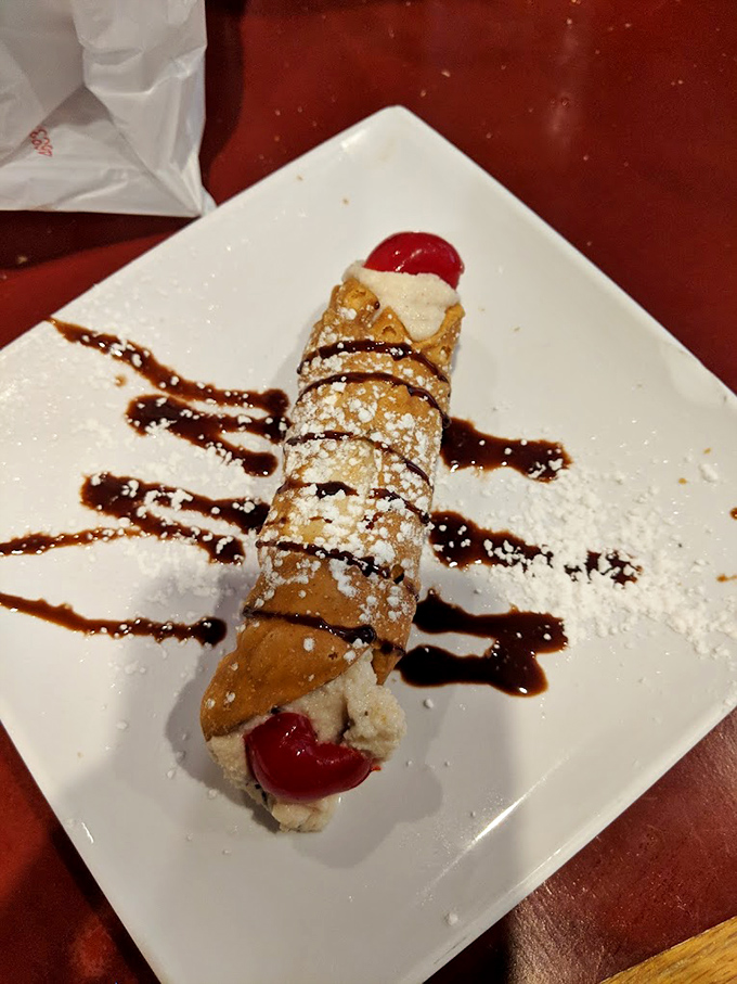 Not just any cannoli&mdash;this crisp shell filled with sweet cream, adorned with chocolate drizzle and cherries, is dessert architecture at its finest.