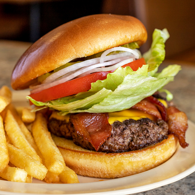 A burger that requires jaw exercises beforehand – stacked with fresh veggies, crispy bacon, and a patty that knows what it's doing.