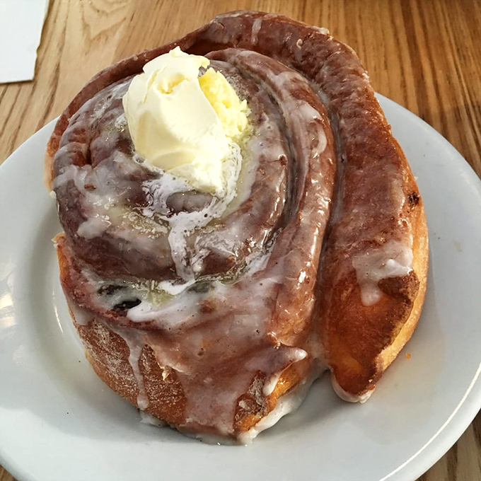 A cinnamon roll that's clearly living its best life, glistening with glaze and sporting a butter hat like it's Derby Day.