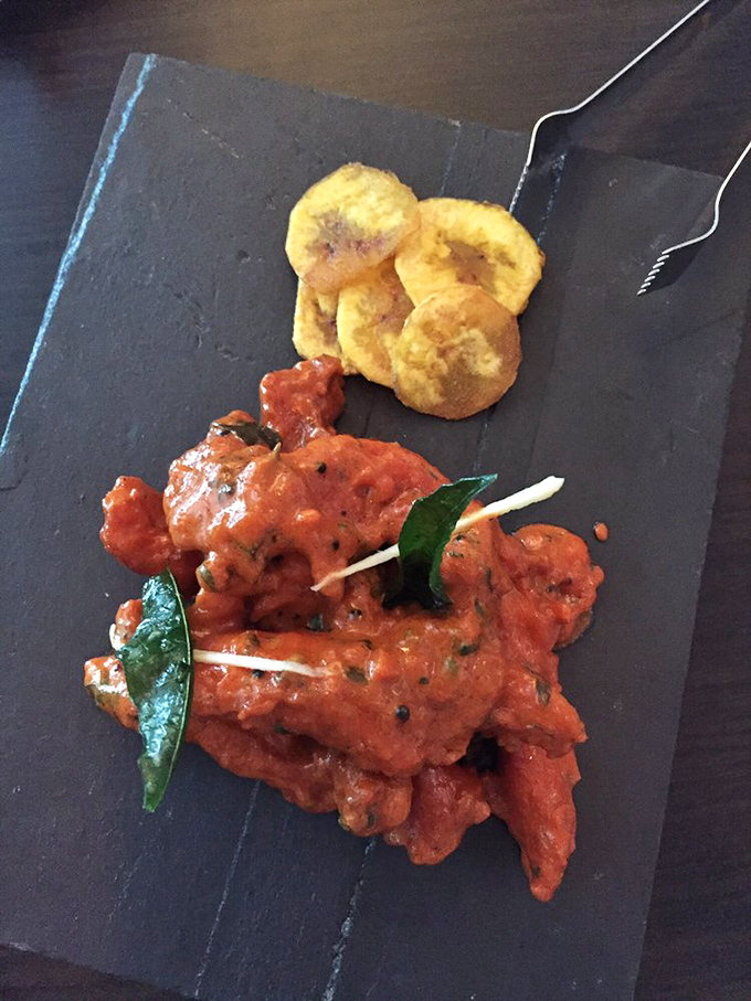 The Coconut Chicken arrives like a spicy sunset on slate&mdash;tender morsels bathed in vibrant sauce with plantain chips standing by for dipping duty.