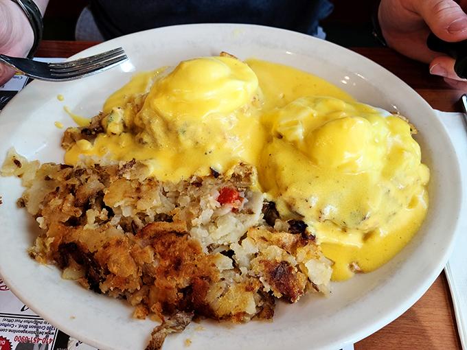 Eggs Benedict draped in hollandaise like they're wearing their Sunday best, with home fries playing the perfect supporting role.