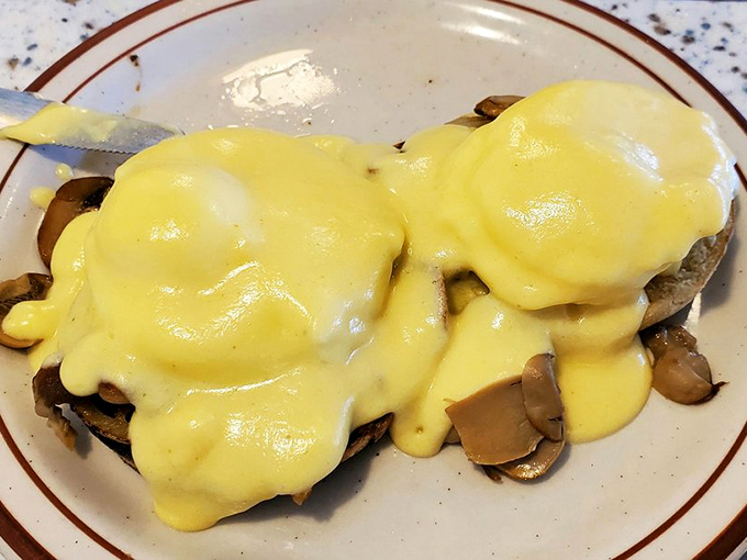 Eggs Benedict draped in hollandaise that cascades like a yellow waterfall over mushrooms. Brunch dreams are made of this.