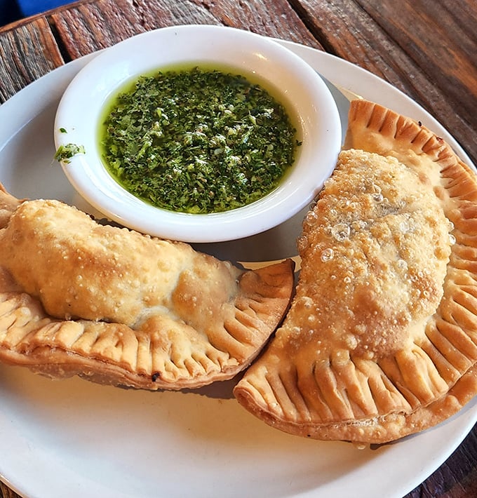 Golden empanadas with that telltale crimped edge, ready for their cilantro sauce bath. Resistance is futile, just accept you'll be ordering seconds.