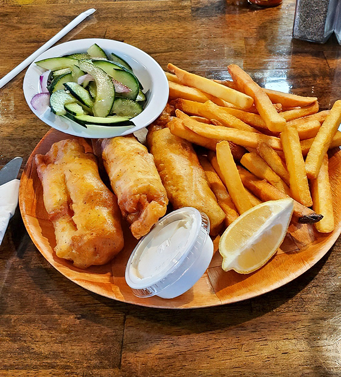 Fish and chips served on a wooden plate with cucumber salad &ndash; proof that simplicity, when done right, is the ultimate sophistication.