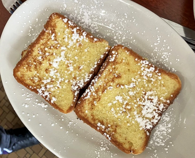 French toast dusted with powdered sugar like fresh snow on a delicious landscape. Two perfect slices waiting for maple syrup's warm embrace.